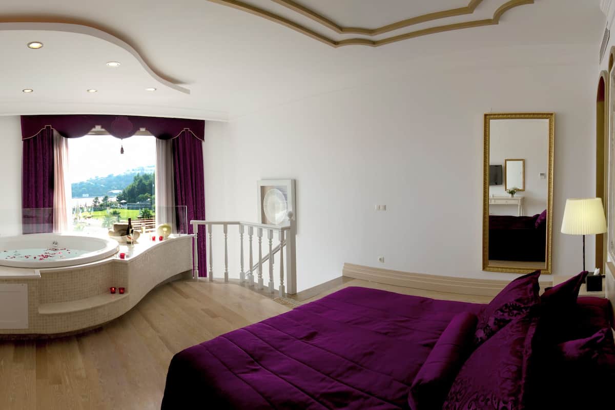 Quarto com uma cama grande, banheiro com banheira e vista para um jardim.
