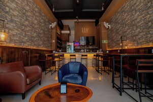 Uma área de bar com paredes de pedra, assentos de couro e um balcão com diversos tipos de garrafas.