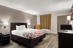 Quarto de hotel com uma cama grande, mesas de cabeceira, uma cadeira, escrivaninha e televisão.