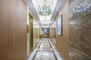 Corredor de hotel com piso de mármore, um candelabro e obras de arte emolduradas nas paredes.