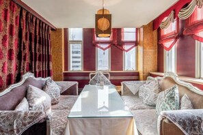 Quarto com mesa de vidro, sofás estampados e cortinas vermelhas.