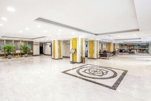Um hall amplo com piso de mármore, balcão de recepção e plantas em vasos.