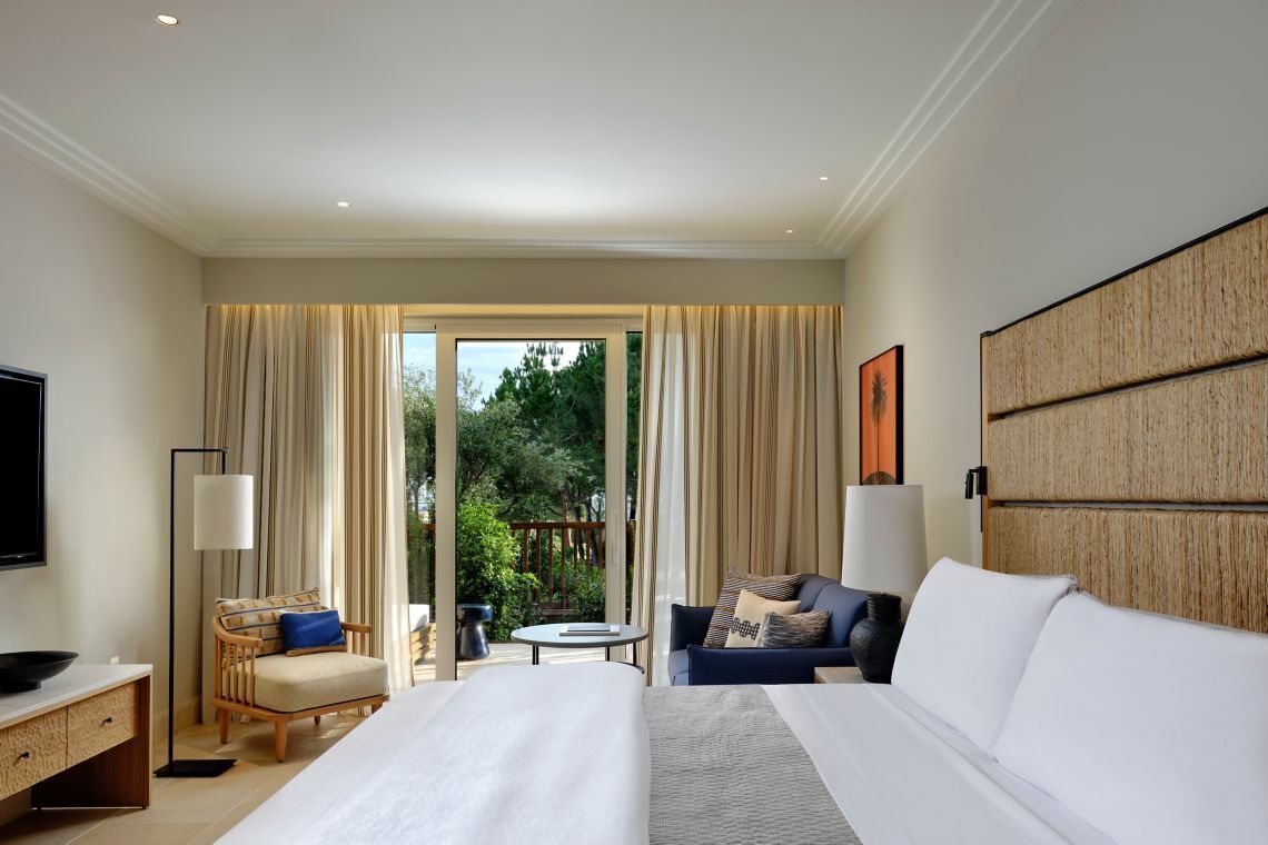 Quarto de hotel com cama grande, sofá, televisão, escrivaninha e vista para o exterior.