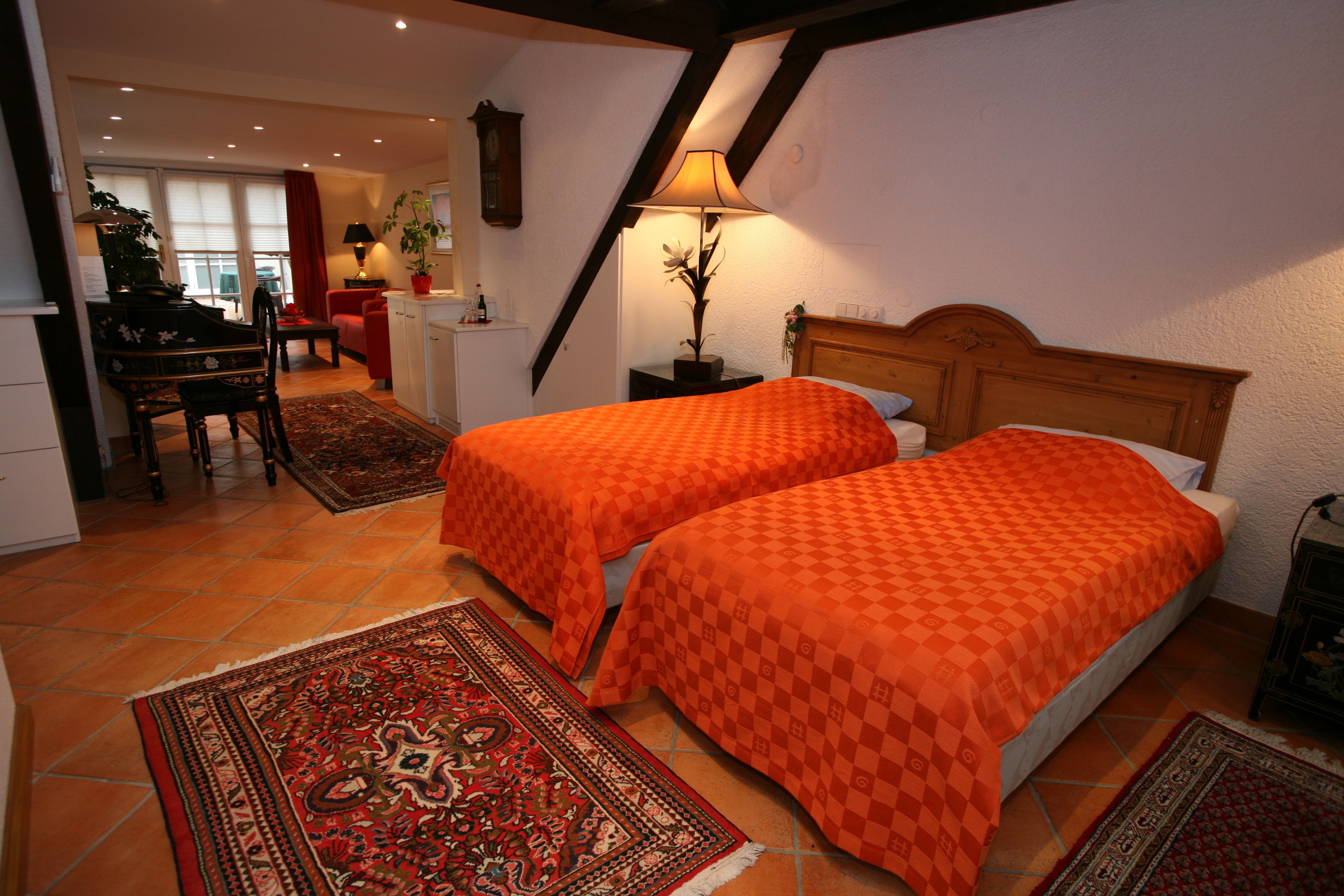 Quarto com duas camas, mesa de cabeceira, luminária, escrivaninha e cadeira.