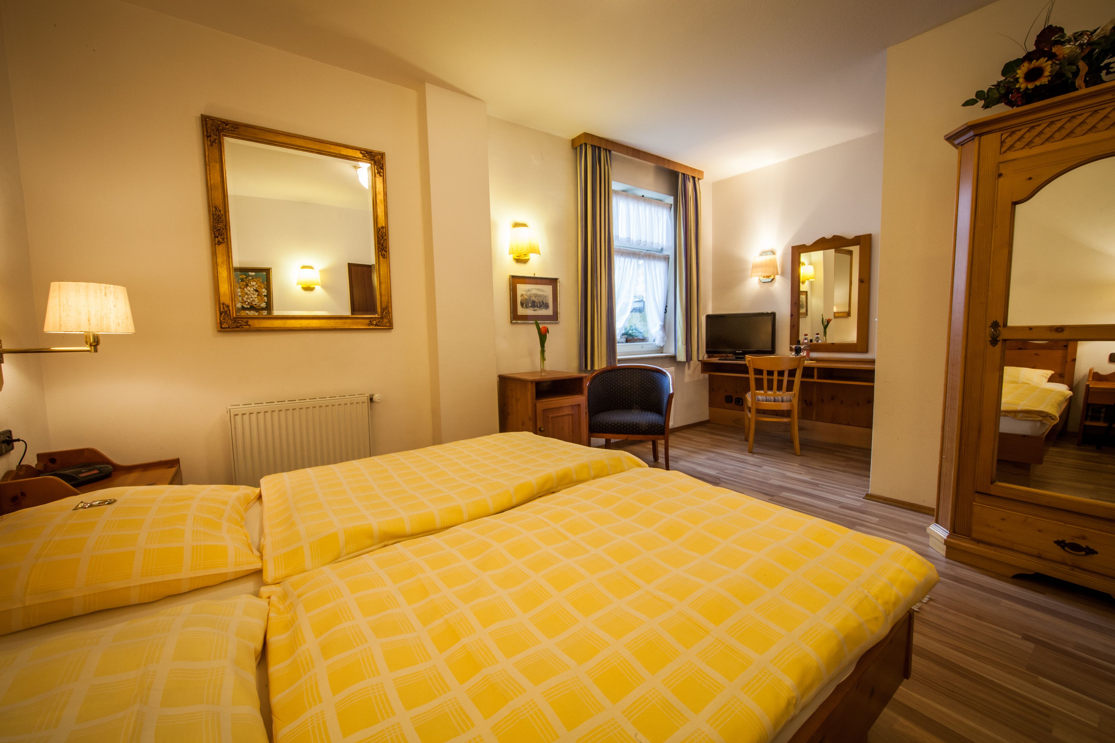 Quarto de hotel com duas camas, uma mesa, uma cadeira, uma televisão e um espelho grande.