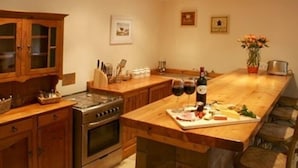 Uma cozinha com armários de madeira, uma ilha central com uma garrafa de vinho e diversos utensílios de cozinha.