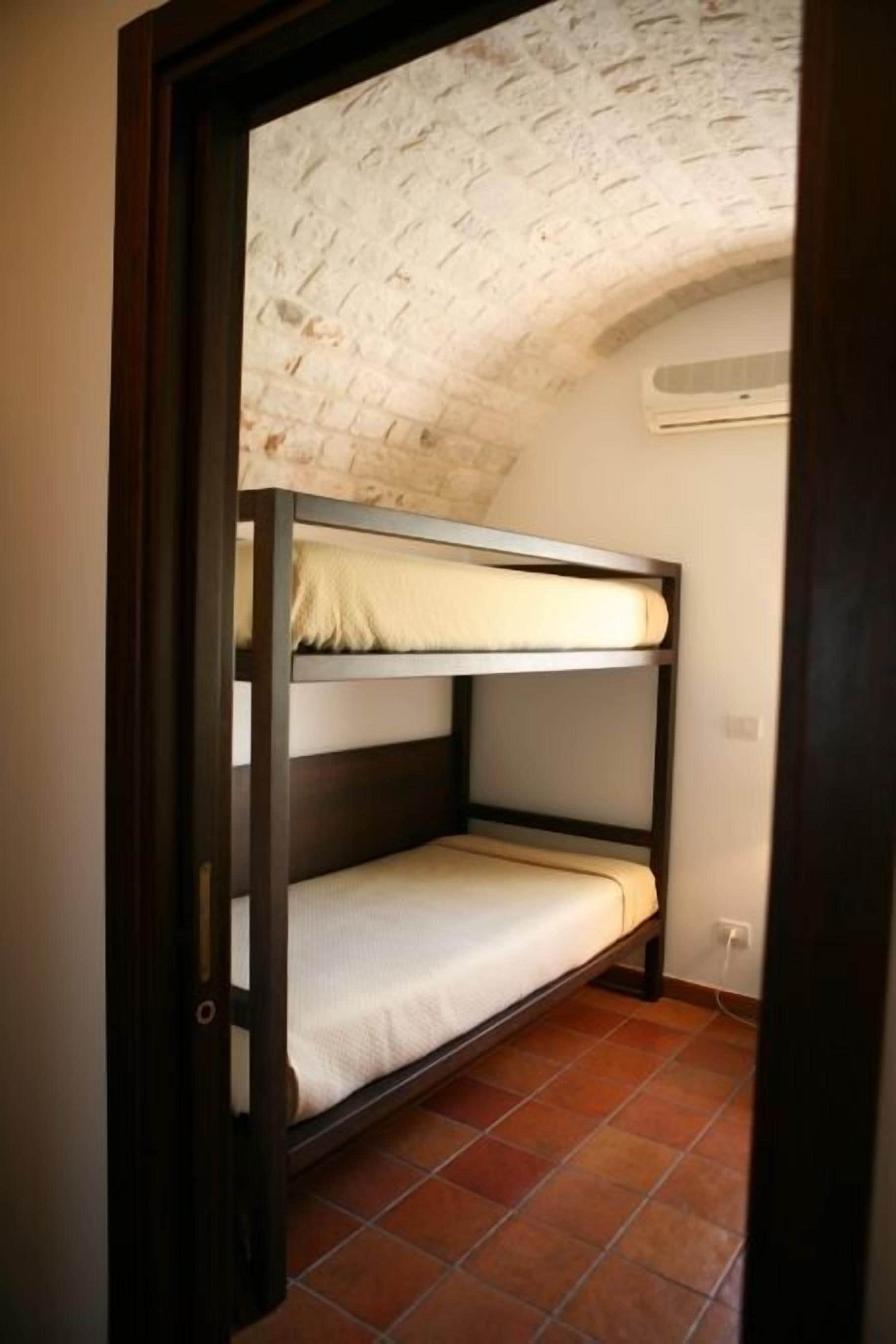 Quarto com beliche, parede de tijolos e chão de azulejos.