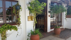 Entrada de um edifício com placa de recepção, placa para hospedaria e plantas em vasos.