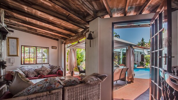 Quarto aconchegante com móveis de vime, vista para uma piscina e teto de madeira.
