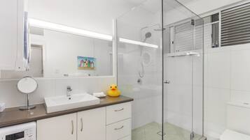 Uma casa de banho moderna com chuveiro em cabine de vidro, lavatório branco e um patinho de borracha no balcão.