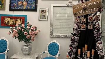 Um quarto com uma parede decorada com diversas obras de arte emolduradas, uma pequena mesa com um vaso de flores e uma exposição de caveiras e velas.