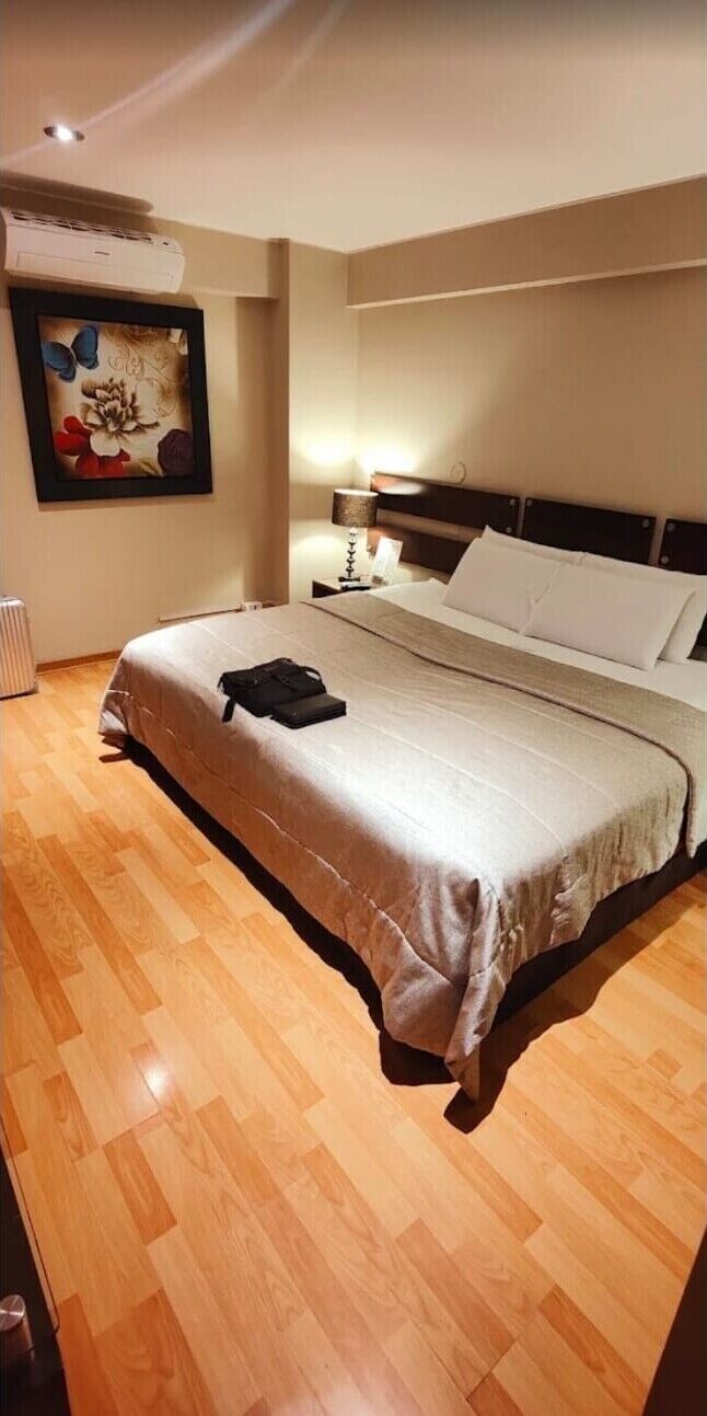 Quarto de hotel com uma cama grande, mesa de cabeceira, luminária e um quadro na parede.