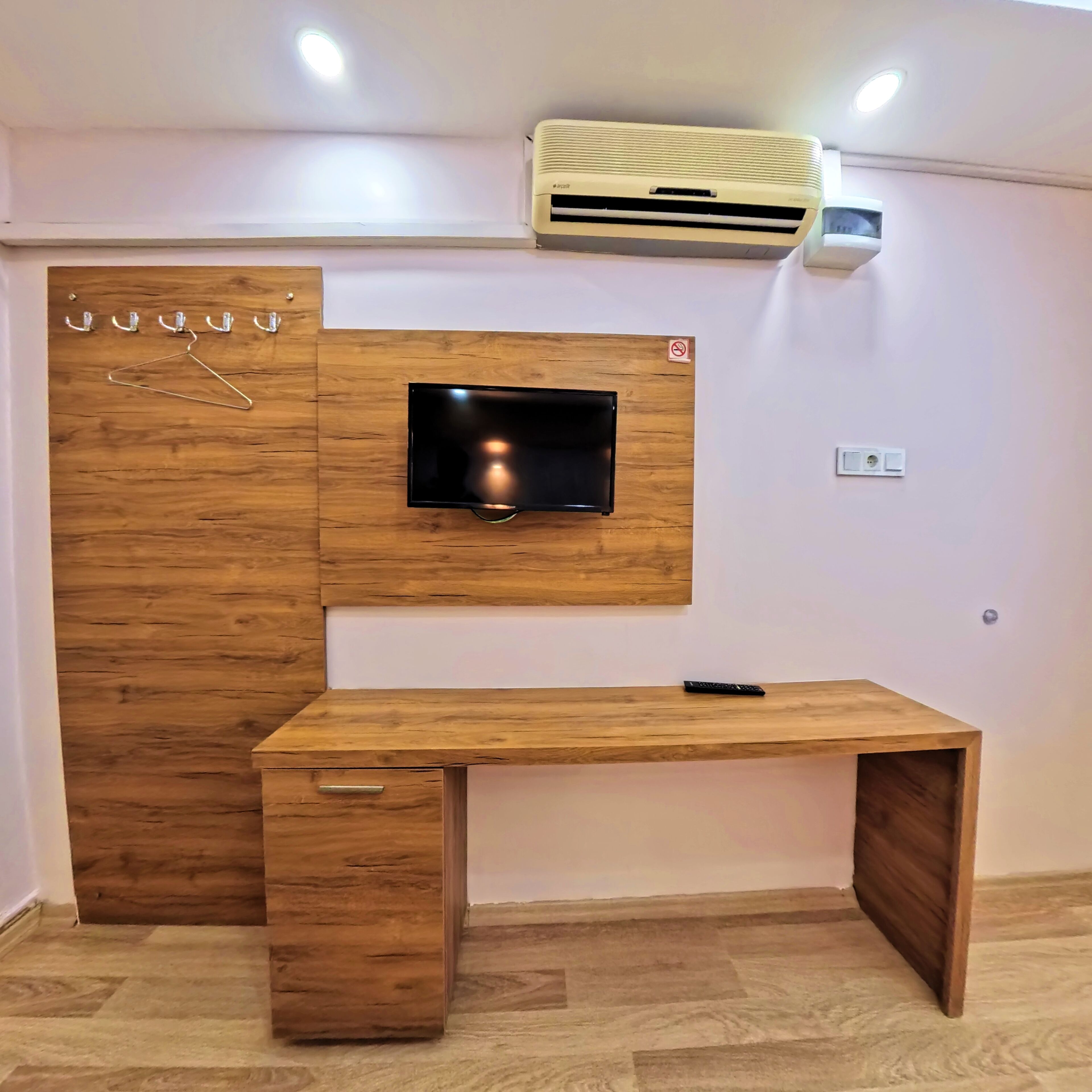 Quarto com escrivaninha de madeira, televisão montada na parede e aparelho de ar condicionado.