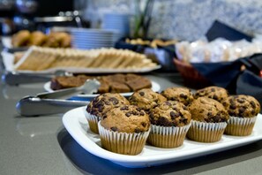 Uma mesa de buffet com diversos produtos de panificação, incluindo muffins e um bolo grande.
