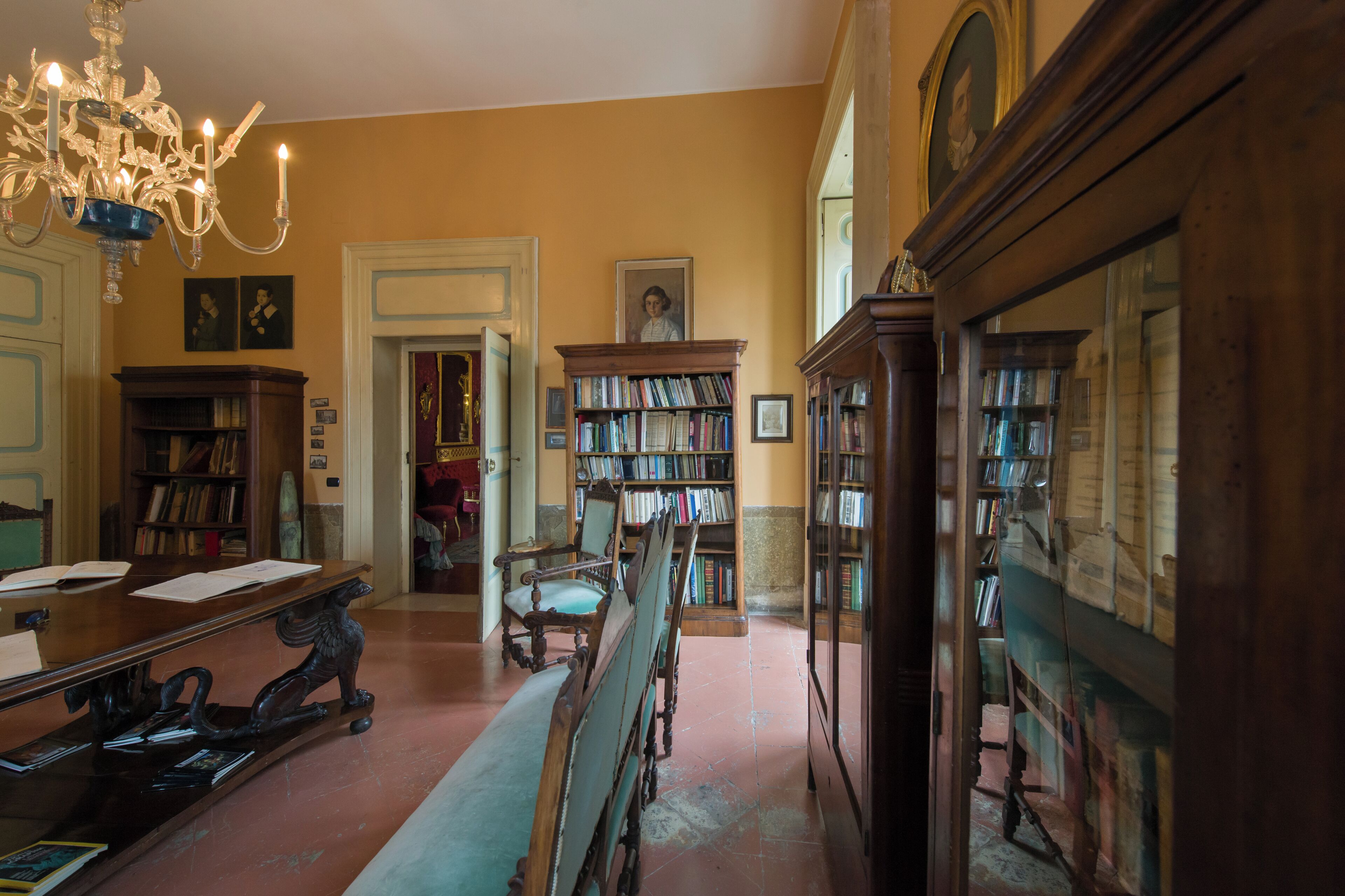 Uma biblioteca com estantes, uma escrivaninha de madeira e um candelabro.