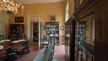 Uma biblioteca com estantes, uma escrivaninha de madeira e um candelabro.