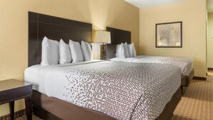 Quarto de hotel com duas camas, uma mesinha de cabeceira, uma luminária e um quadro na parede.