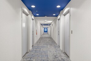 Um corredor de hotel com paredes brancas, teto azul e piso coberto de carpete.
