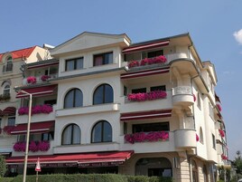 Um hotel de vários andares com varandas decoradas com flores cor-de-rosa, janelas em arco e toldo vermelho.