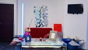 Uma sala de estar moderna com um sofá vermelho, uma mesa de centro de vidro e uma obra de arte abstrata singular na parede.