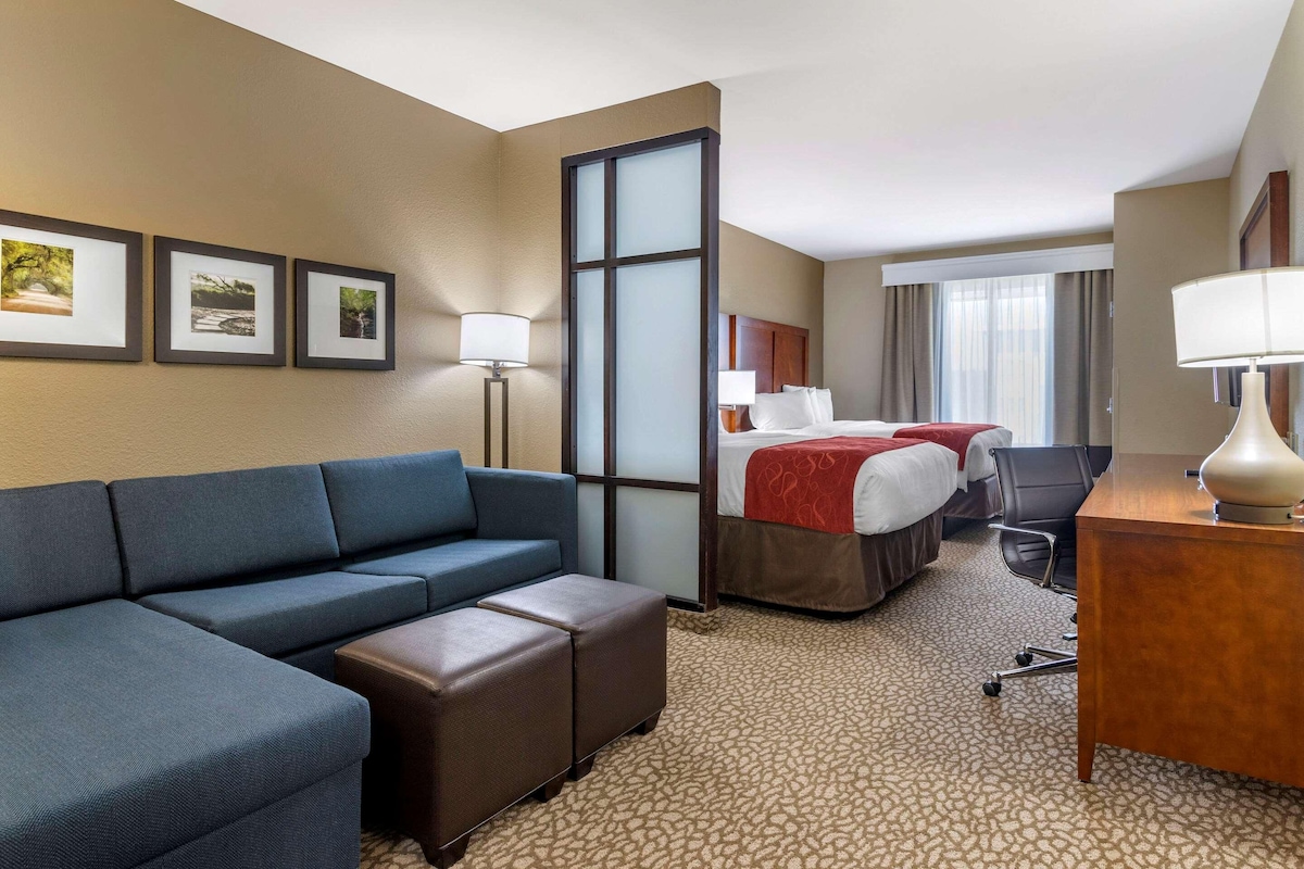 Quarto de hotel com sofá, cama, escrivaninha e cadeira. Há três quadros na parede.