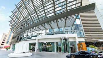 Um edifício moderno com fachada de vidro, entrada destacada com porta giratória e um carro preto estacionado na frente.