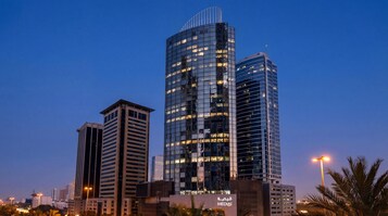 Um edifício moderno e alto com fachada de vidro, cercado por outros edifícios imponentes.