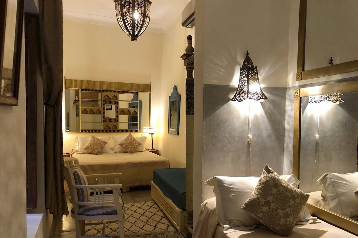 Quarto de hotel com cama, cadeira, espelho e iluminação decorativa.