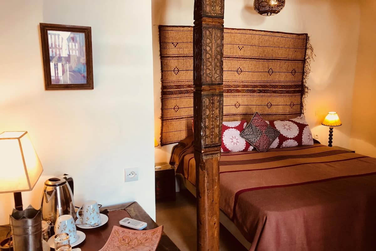 Quarto aconchegante com cama, mesa de cabeceira com abajur e um quadro na parede.