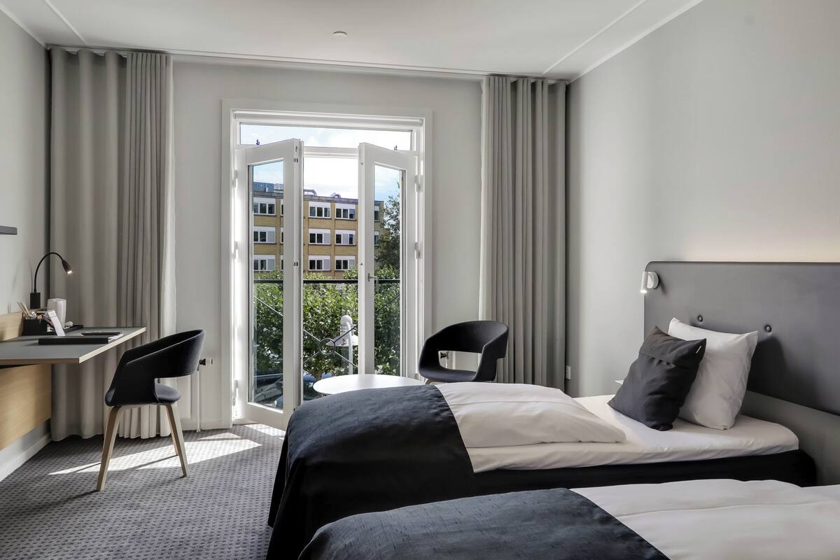 Quarto de hotel com duas camas, uma mesa e uma cadeira.