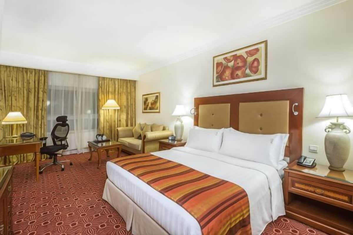 Quarto de hotel com uma cama grande, uma mesa de escritório com cadeira, um sofá e duas luminárias.