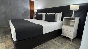 Quarto de hotel moderno com uma cama grande, uma mesa de cabeceira, um abajur e piso de madeira.