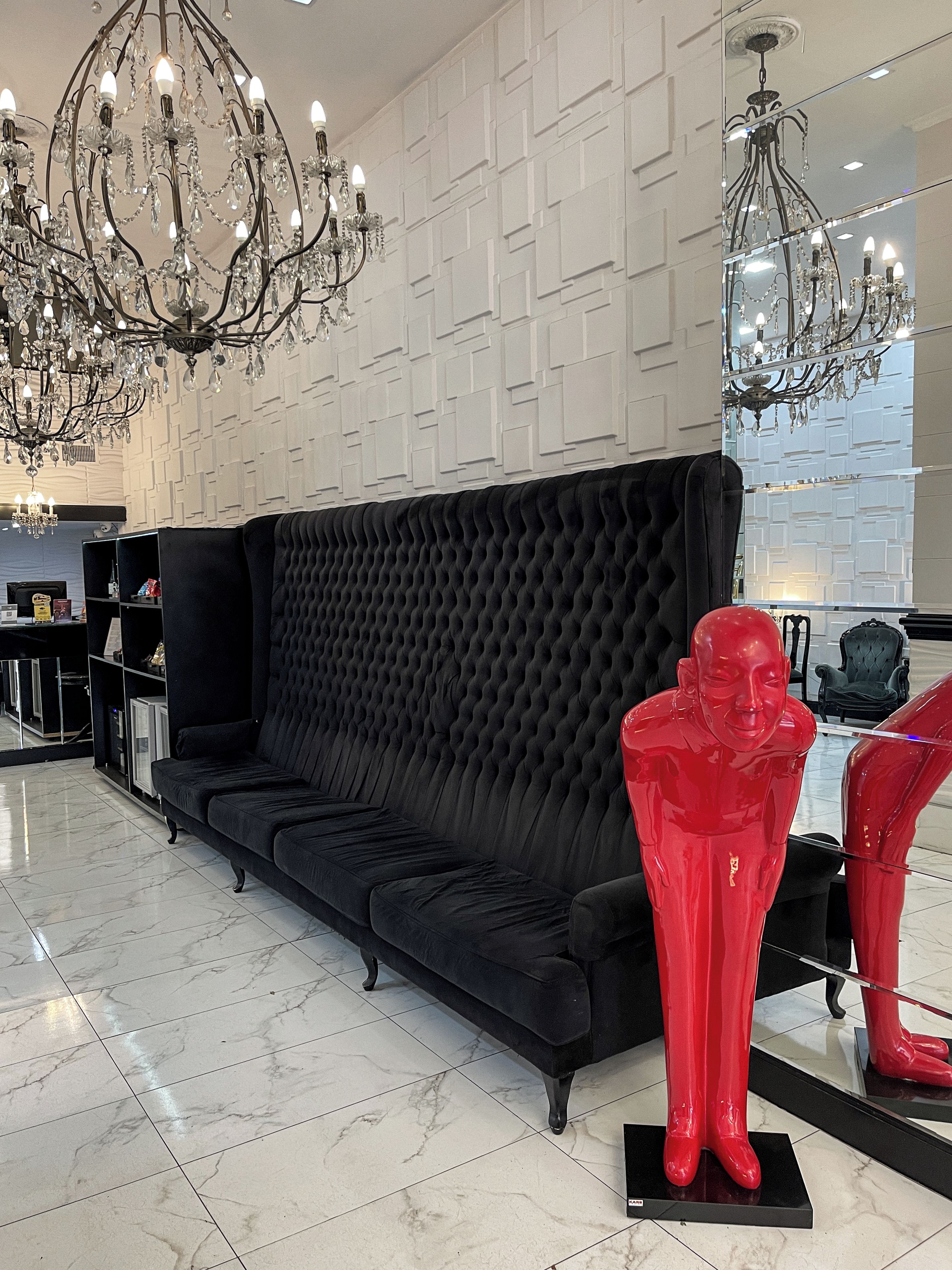 Decoração moderna com sofá preto, lustre e estátuas vermelhas.