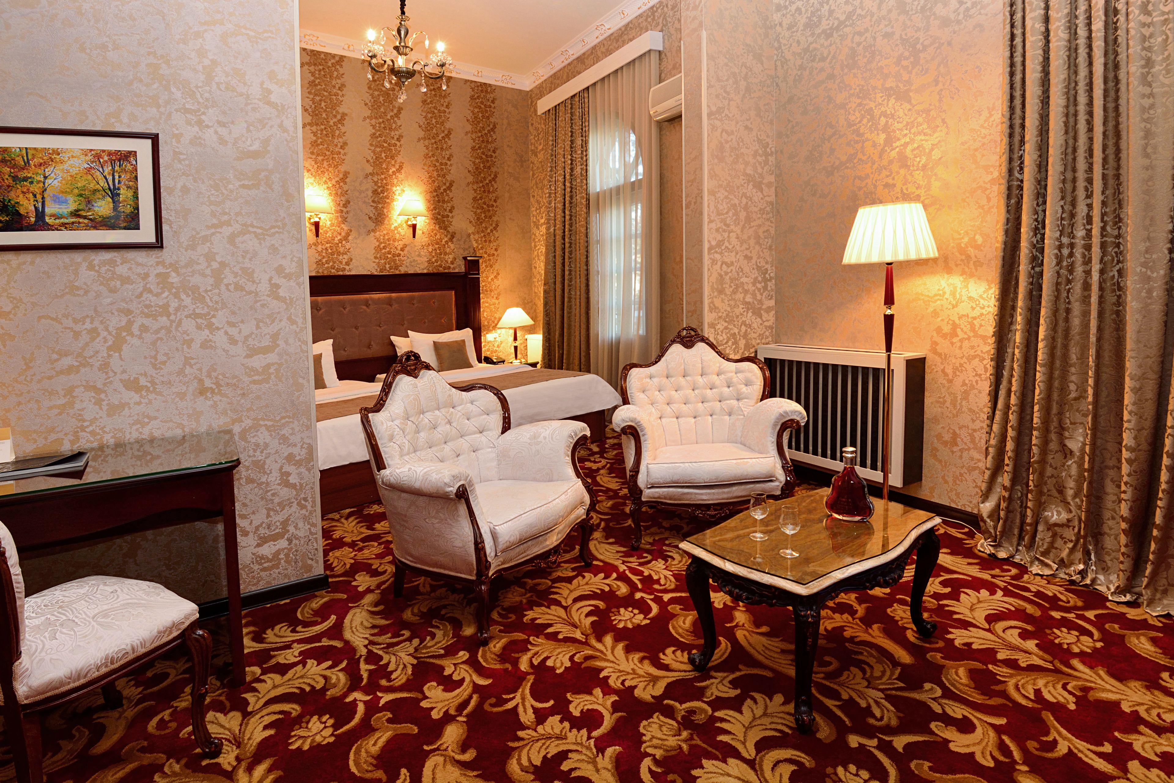 Quarto de hotel com uma cama grande, dois poltronas, uma mesa pequena e uma escrivaninha com uma cadeira.