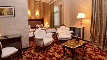 Quarto de hotel com uma cama grande, dois poltronas, uma mesa pequena e uma escrivaninha com uma cadeira.