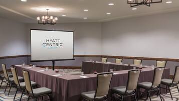 Uma sala de conferências com uma grande tela exibindo "HYATT CENTRIC PARK CITY", uma mesa comprida com cadeiras e um lustre.