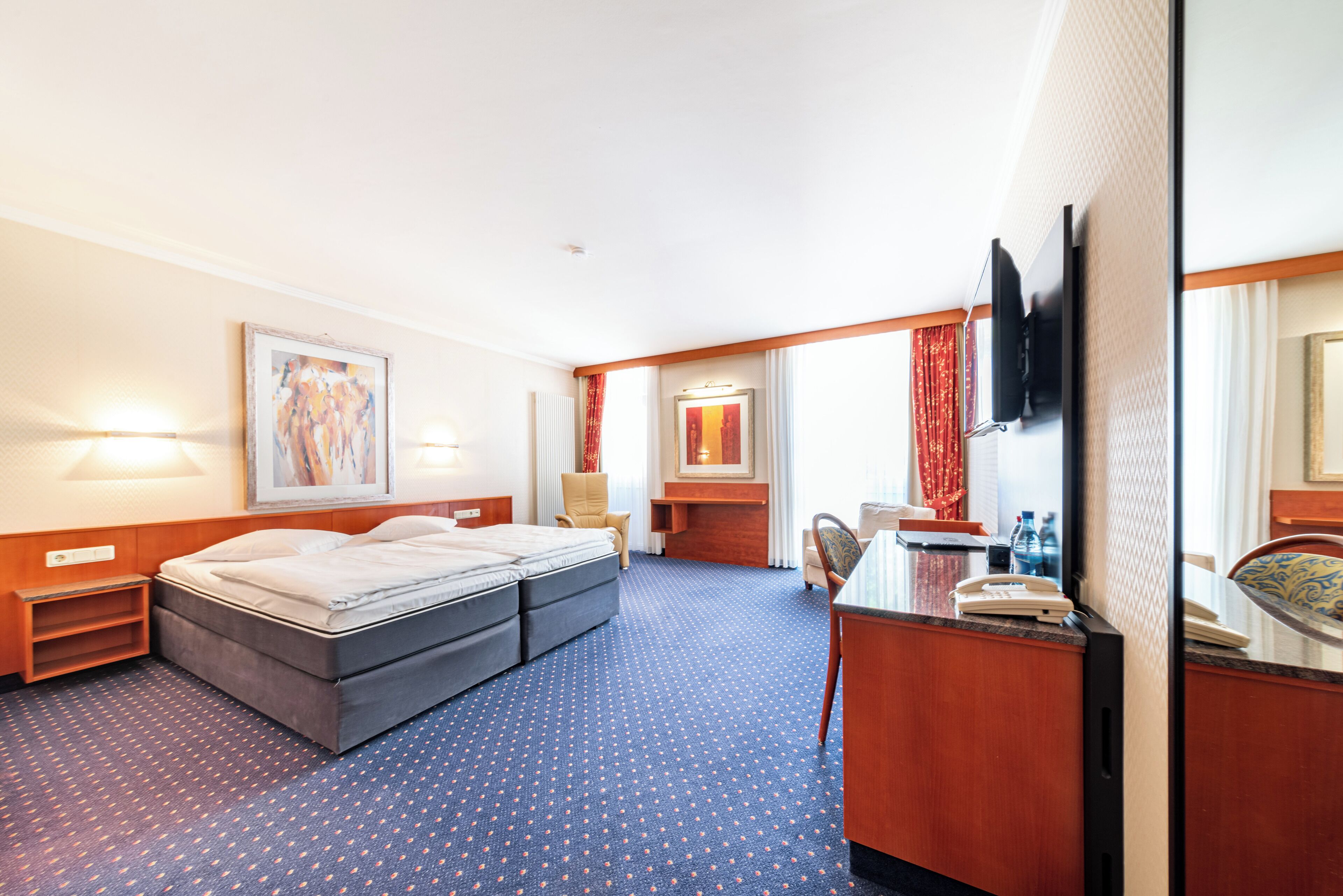 Quarto de hotel com uma cama de casal, uma mesa com telefone, uma cadeira e uma televisão.