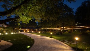 Uma passagem pavimentada num parque à noite, com luzes de corda e iluminada por pequenos focos no chão.