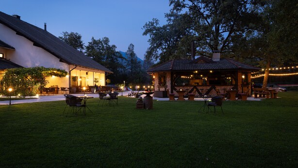 Uma área de pátio ao ar livre com mesas, cadeiras, um gazebo e luzes de corda.