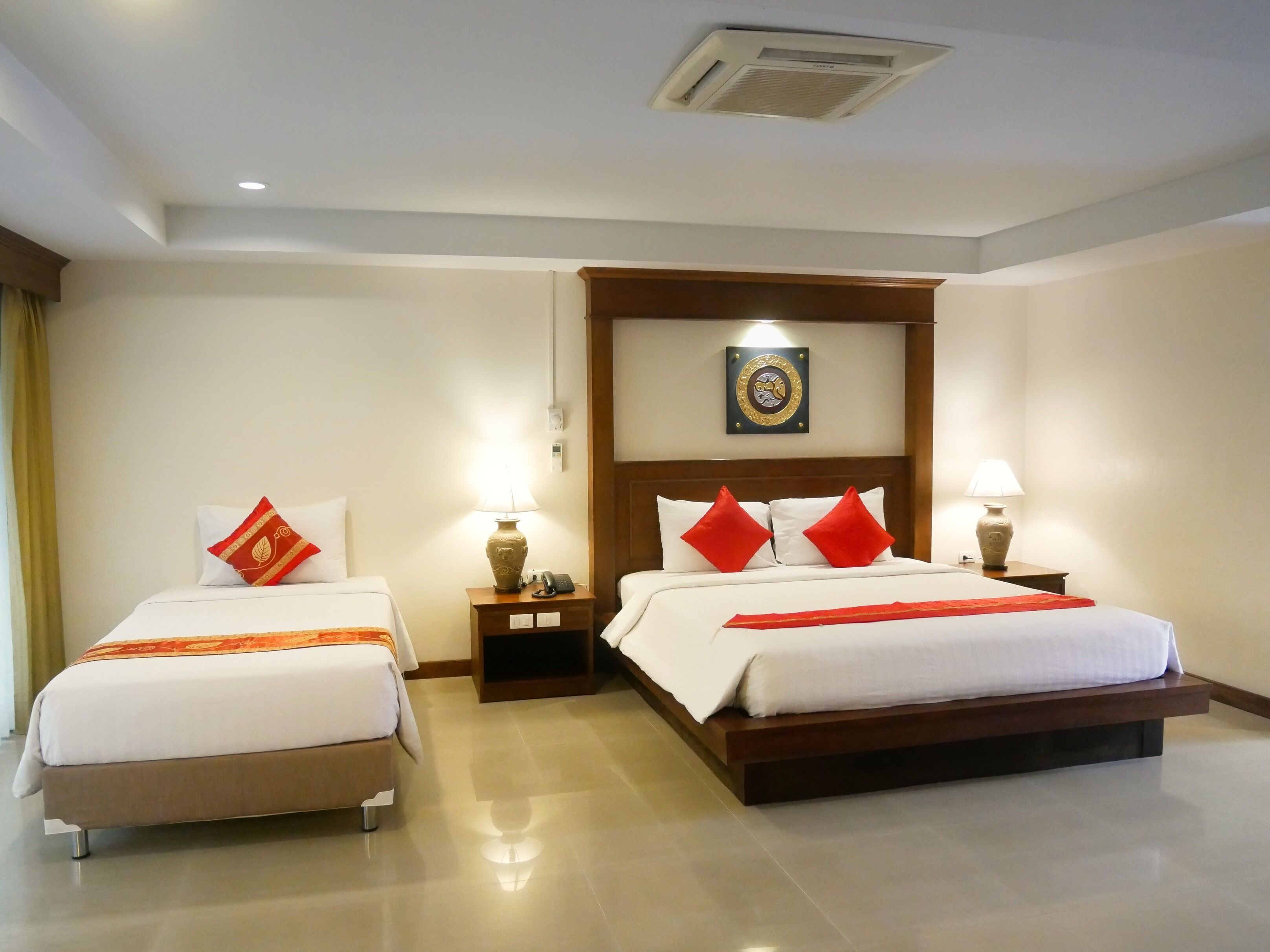 Quarto de hotel com duas camas de solteiro, cabeceira de madeira, mesa de cabeceira com luminária e ar-condicionado fixado na parede.