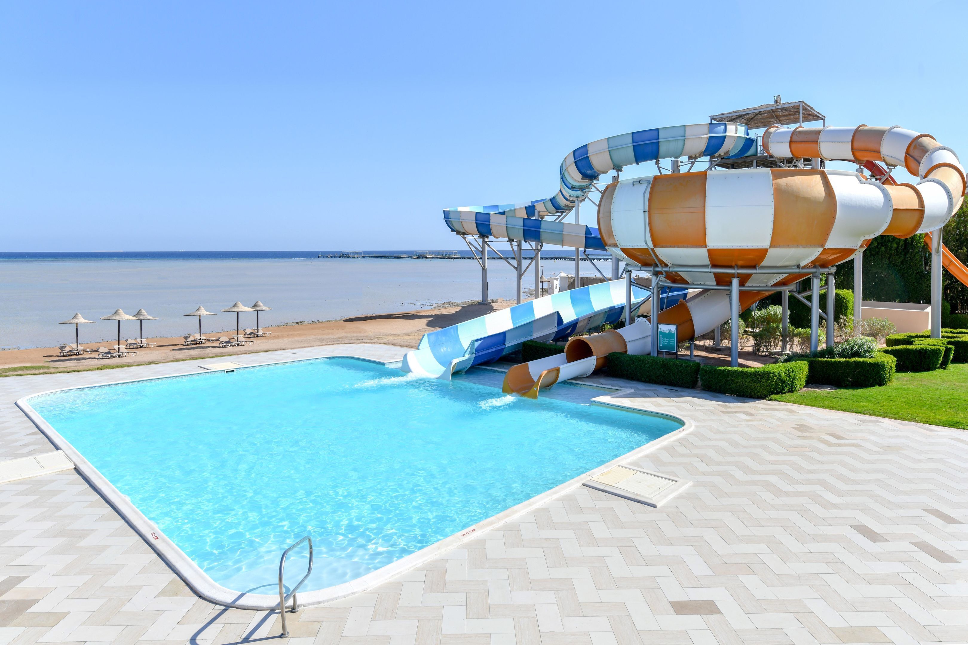 Uma piscina com escorregador, praia e espreguiçadeiras.