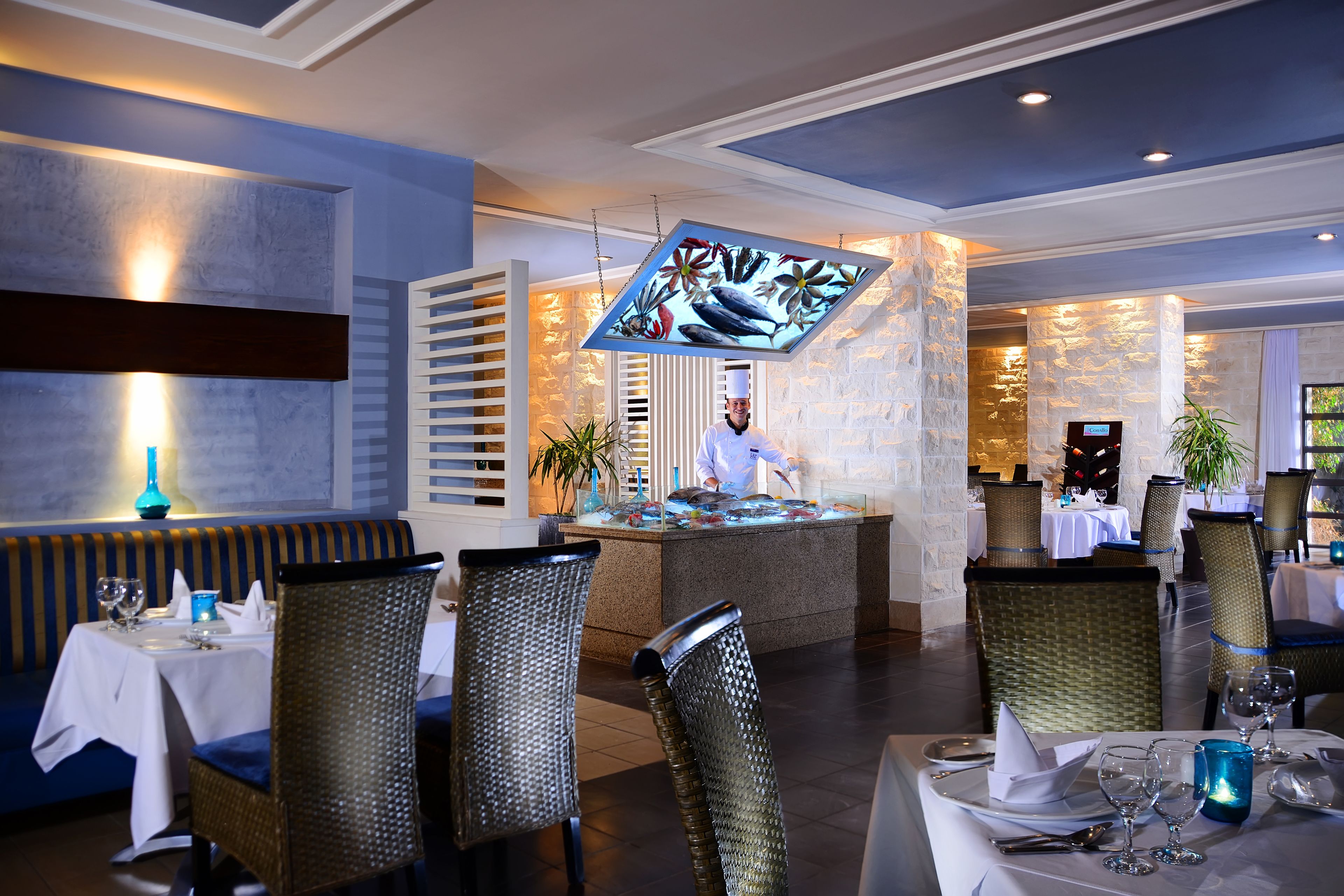 Um restaurante com um cozinheiro no balcão, cadeiras de vime e decoração de interiores moderna.