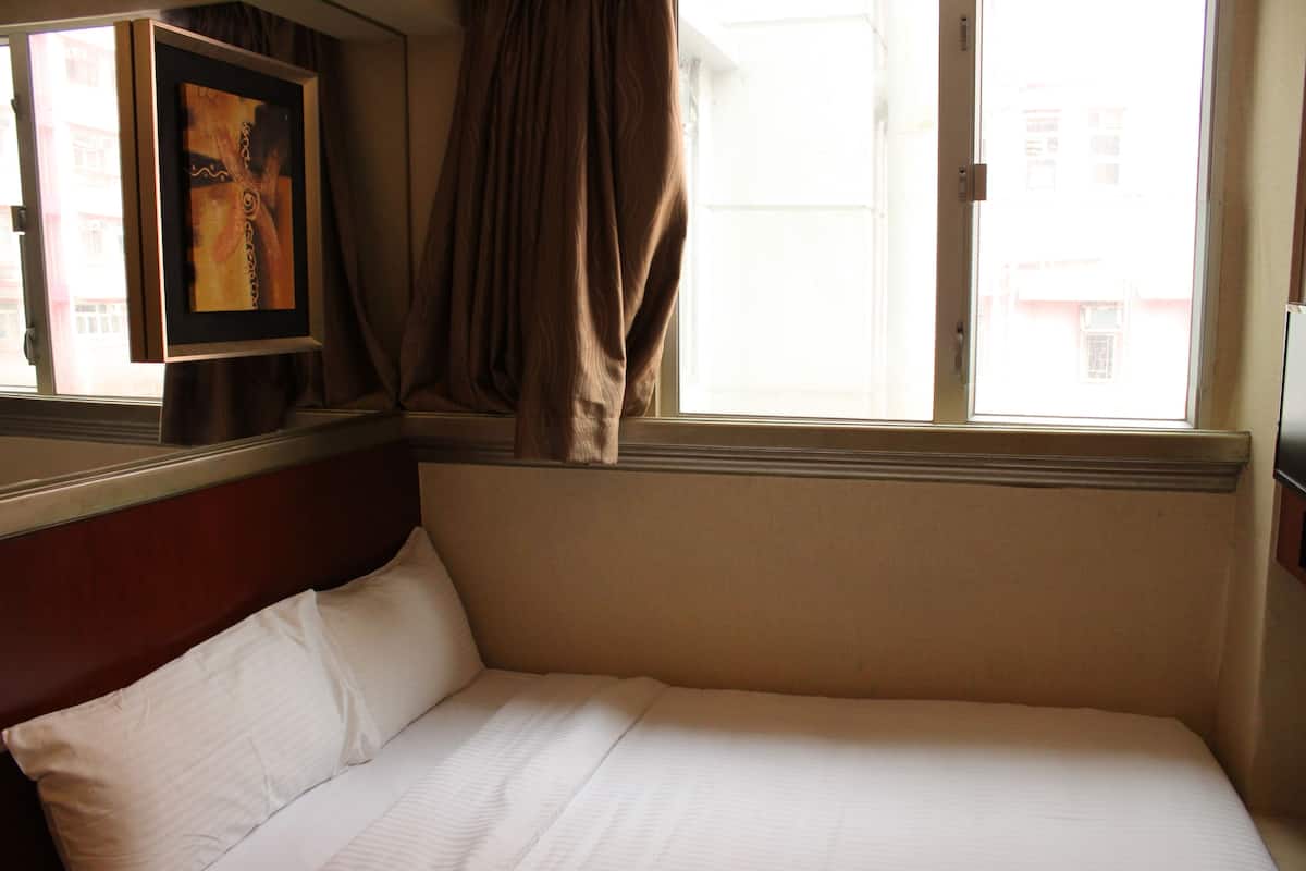 Quarto de hotel com cama, janela com cortinas e quadro na parede.