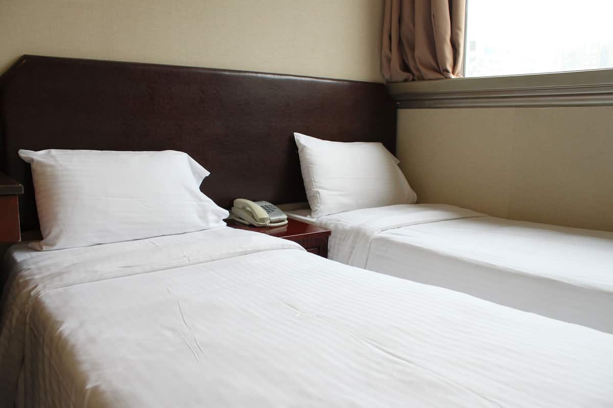 Quarto de hotel com duas camas de solteiro, telefone ao lado da cama e janela com cortinas.