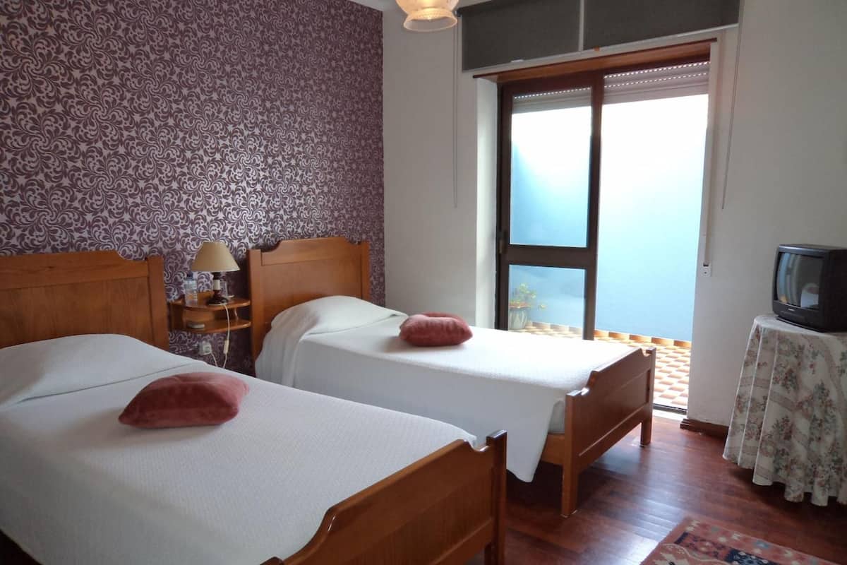 Quarto com duas camas de madeira, uma mesa pequena com uma televisão e uma janela com vista para o mar.