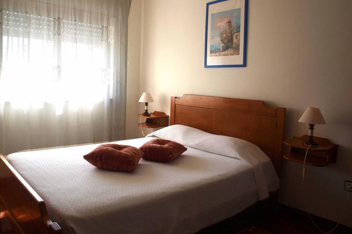 Uma cama bem arrumada com duas almofadas, uma cabeceira de madeira e duas mesas de cabeceira com luminárias.