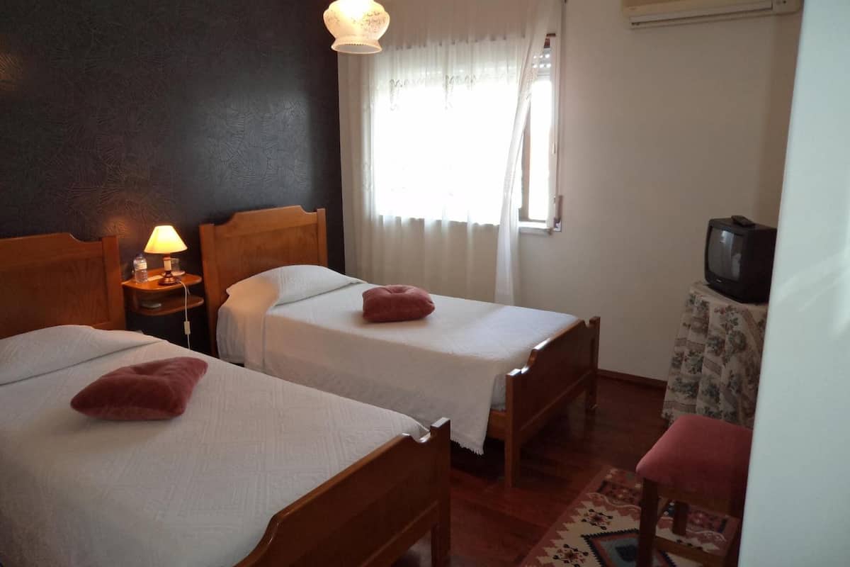 Quarto com duas camas de madeira, uma mesa pequena com televisão e uma janela com cortinas.
