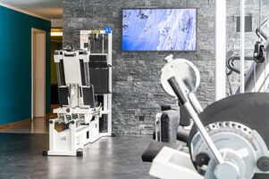 Uma academia com equipamentos de ginástica, uma televisão na parede e uma parede de pedra.