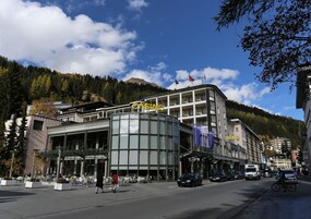 Um hotel moderno com fachada de vidro, área de estar externa e bandeiras que identificam várias marcas.