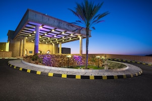 Um edifício com entrada coberta, pilares de pedra e um jardim com uma palmeira.